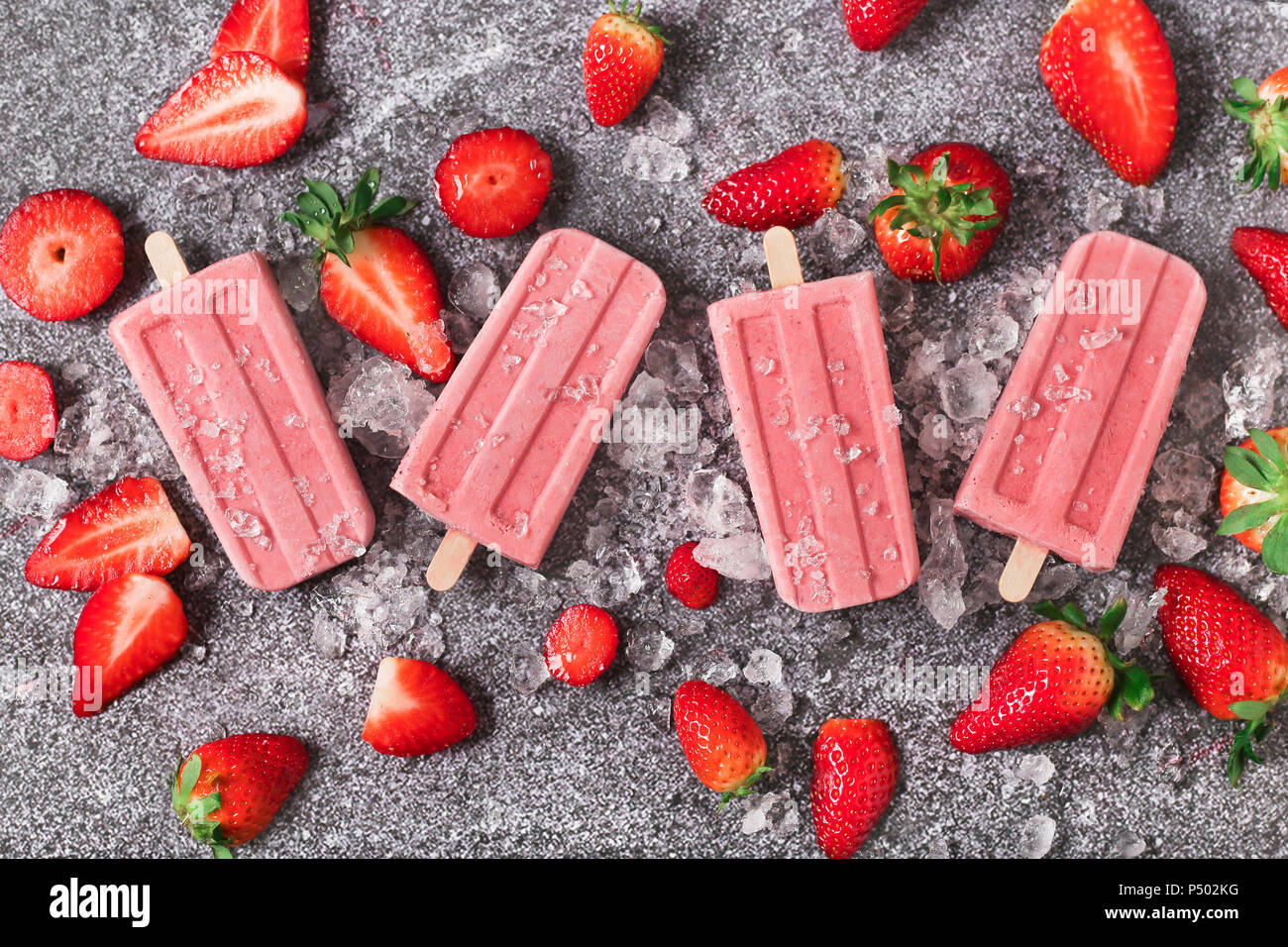Four homemade strawberry ice lollies, ice and strawberries on marble ...