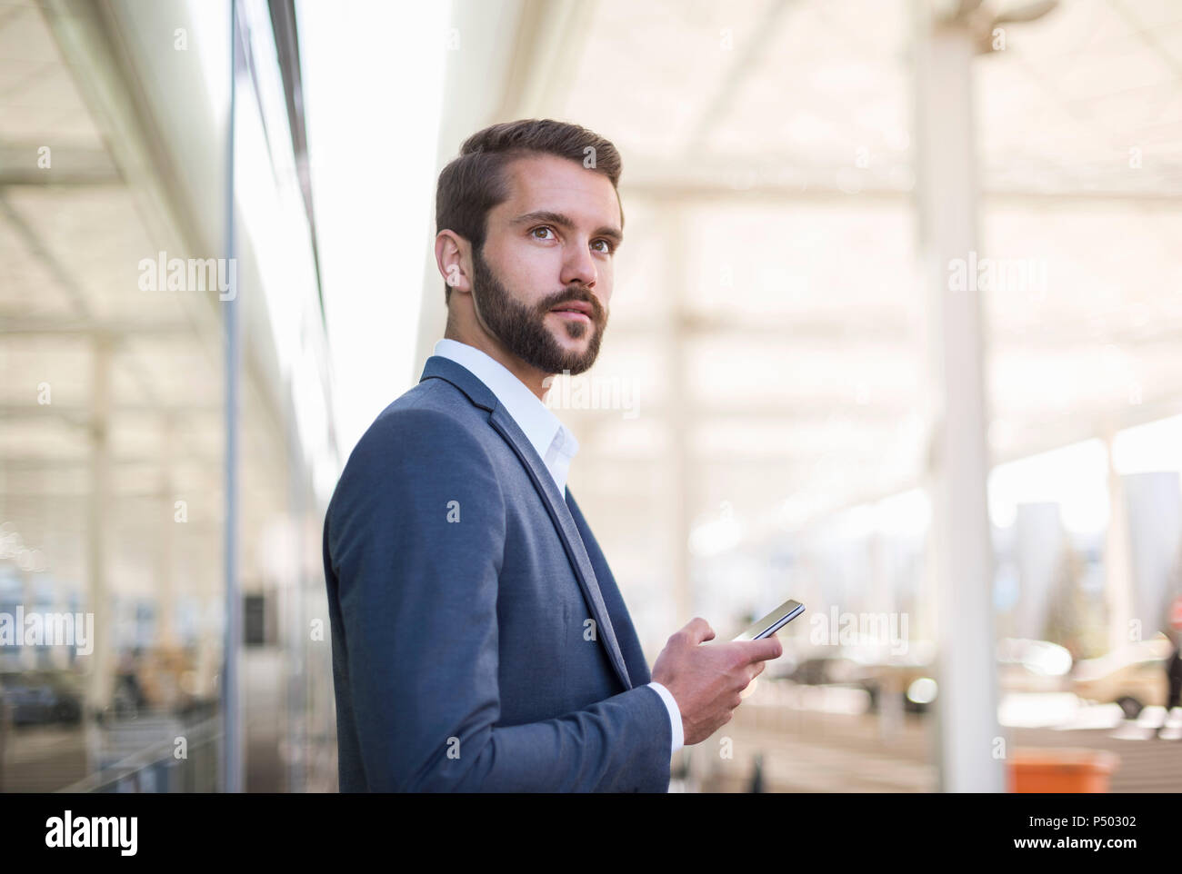 Young businessman holding cell phone looking sideways Stock Photo - Alamy