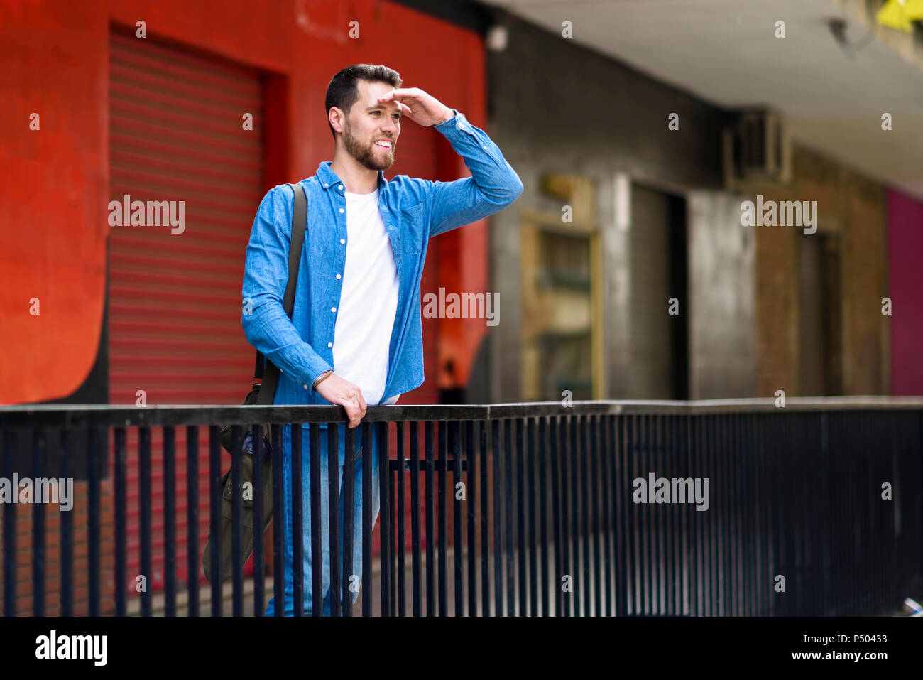Young man standing in the city, looking at distance, shielding eyes ...