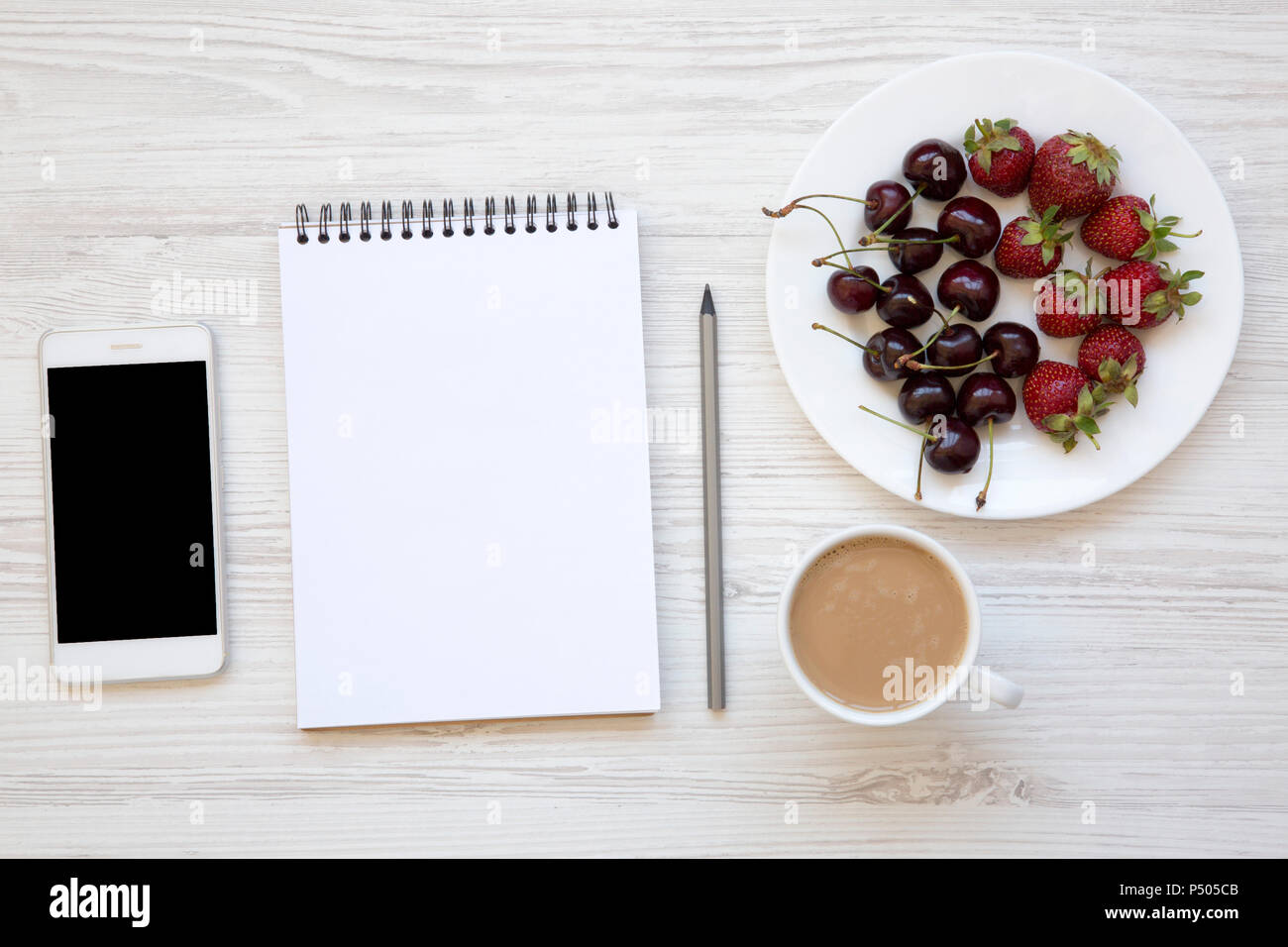 Work space with smartphone, strawberries, cherries, notepad and latte ...