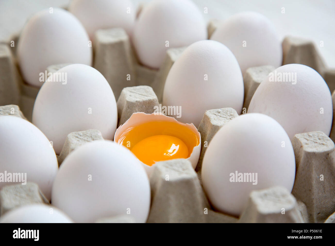 Cracked egg among other chicken eggs in carton egg box, side view Stock ...