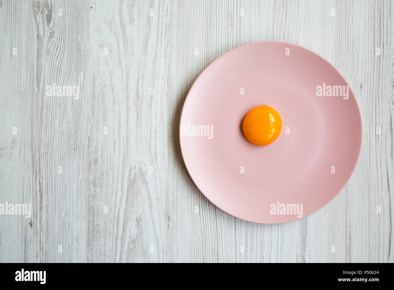 Egg yolk on a pink plate on a white wooden background, top view. Copy ...