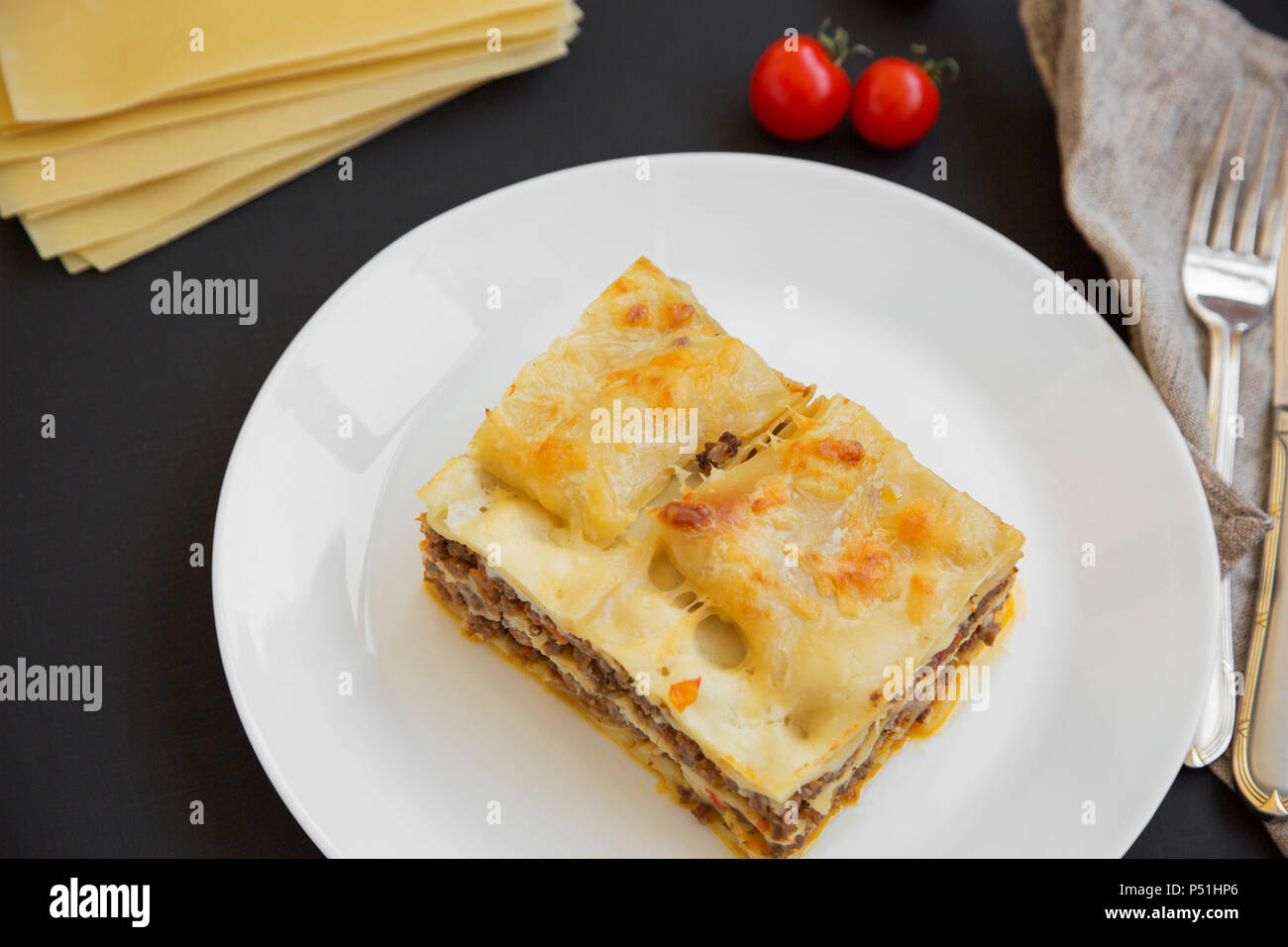 Traditional beef lasagne on a white round plate, black background, top ...