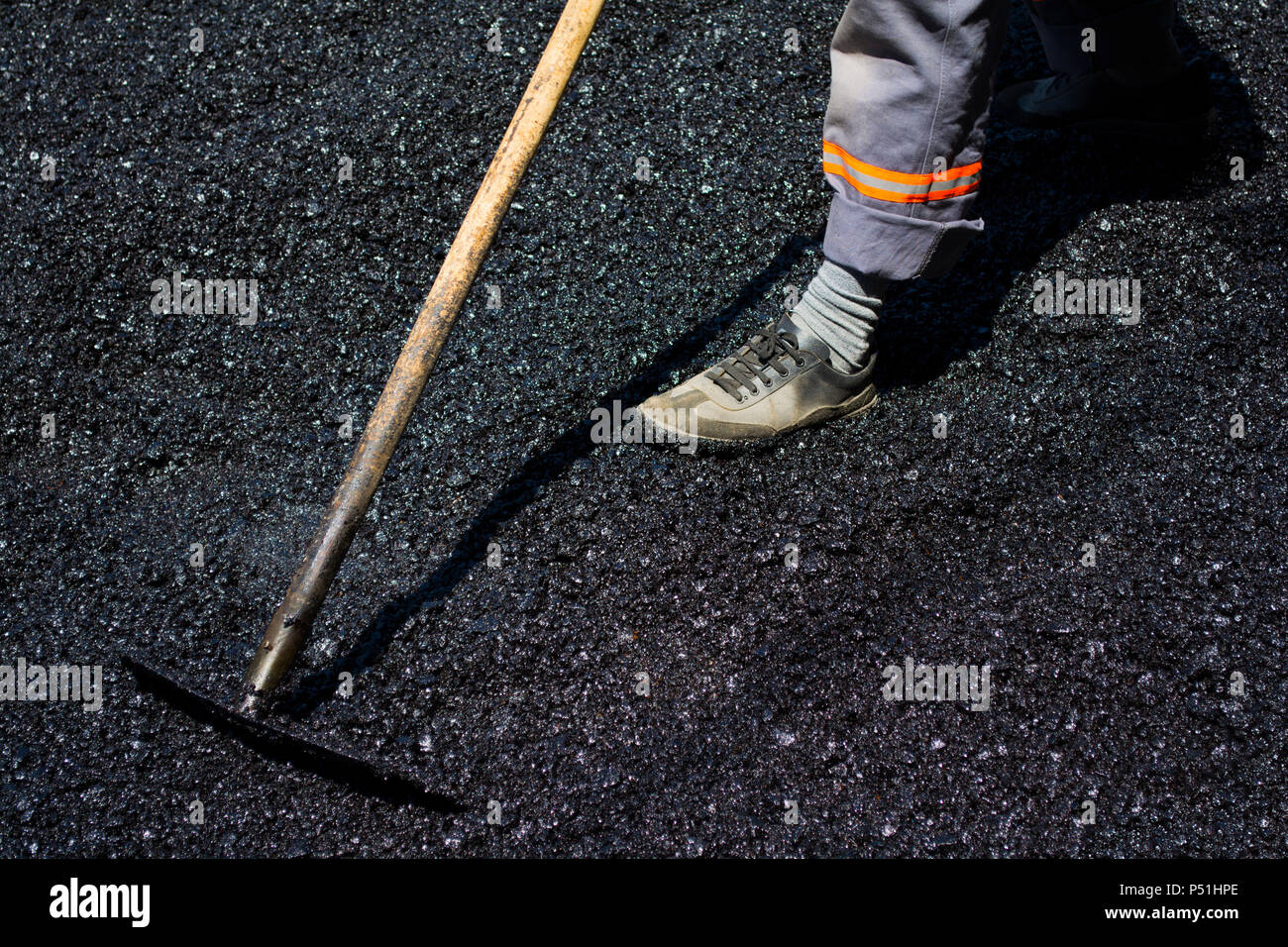 Worker leveling fresh asphalt on a road construction site, industrial ...