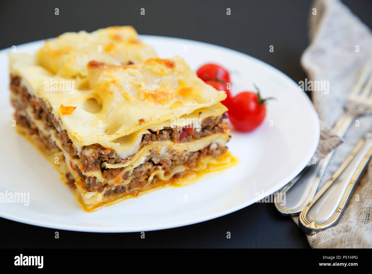 Traditional beef lasagne on a white round plate on black background ...