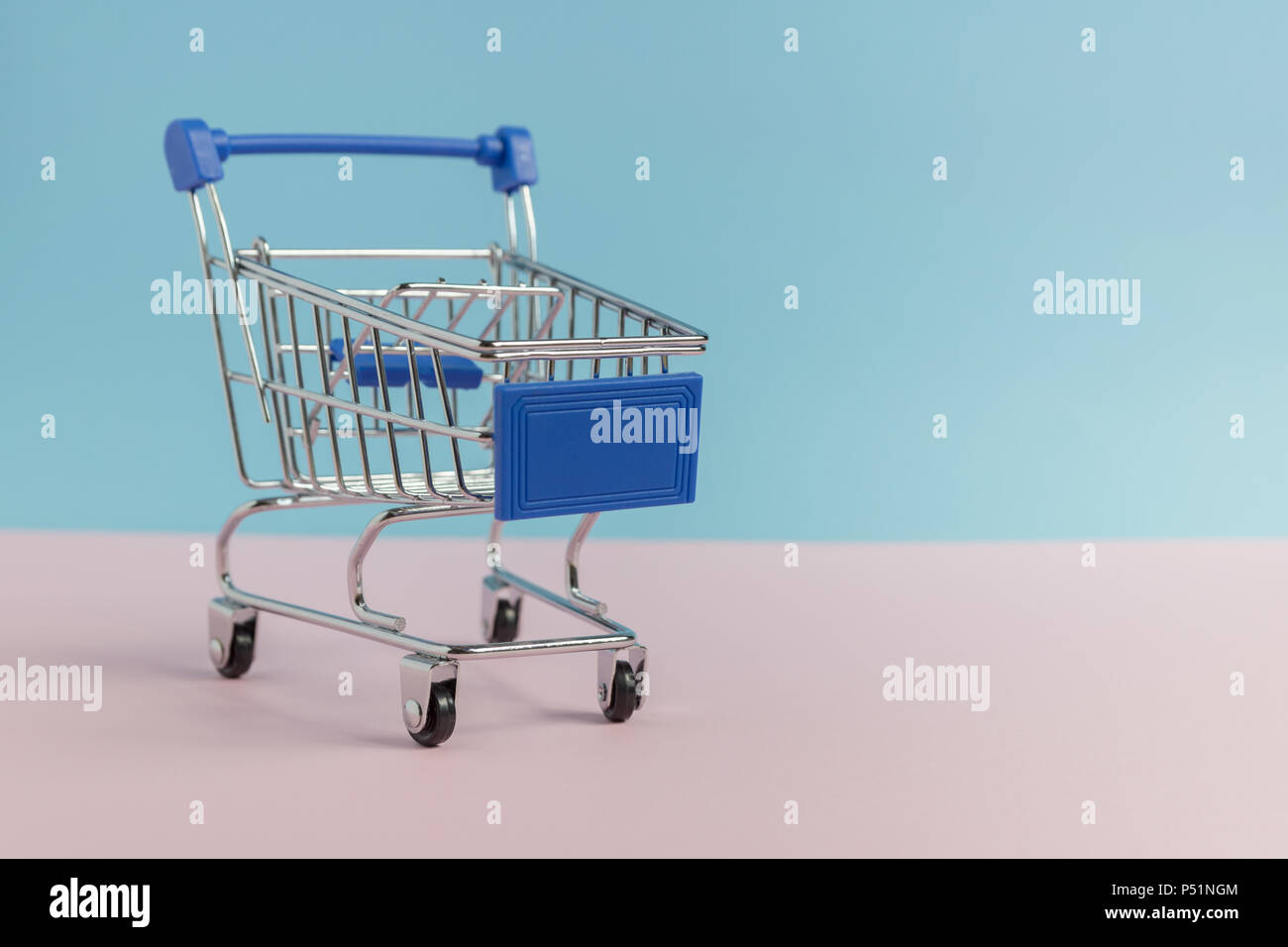 Small empty shopping cart/trolley on half pink, half blue pastel ...