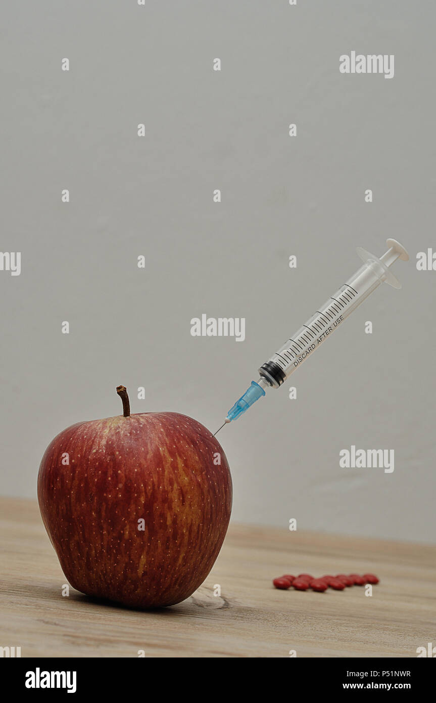 An injection needle stuck into an apple with red pills Stock Photo - Alamy
