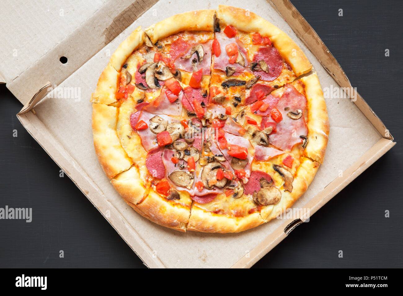 Top view, freshly baked pizza in a cardboard box on dark background ...