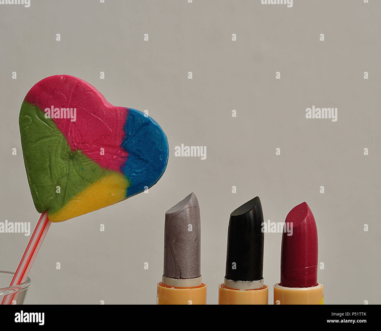 A row of lip sticks displayed with a colorful heart shape lollipop ...