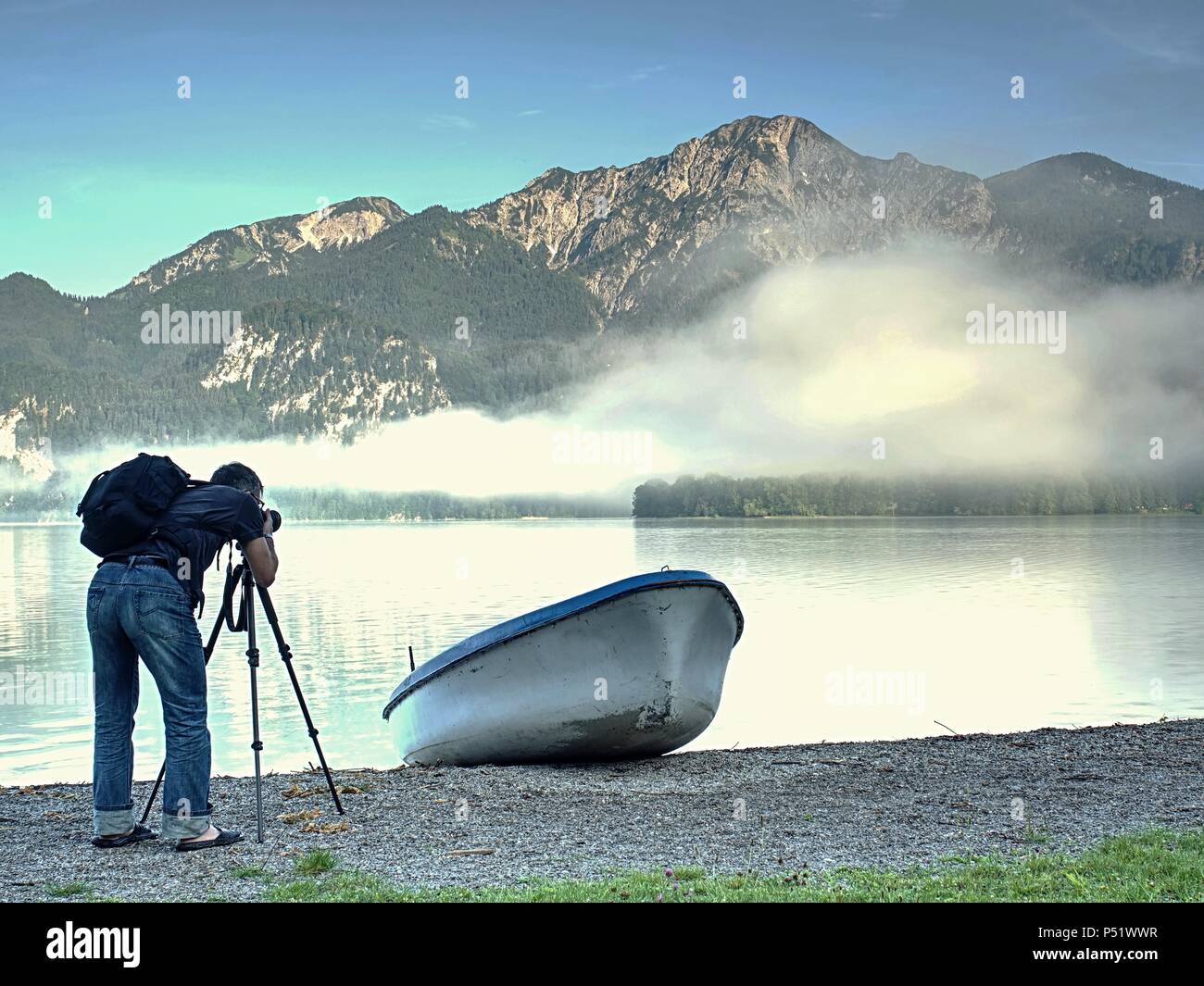 Photographer with eye at viewfinder is taking photo of lake with Alps ...