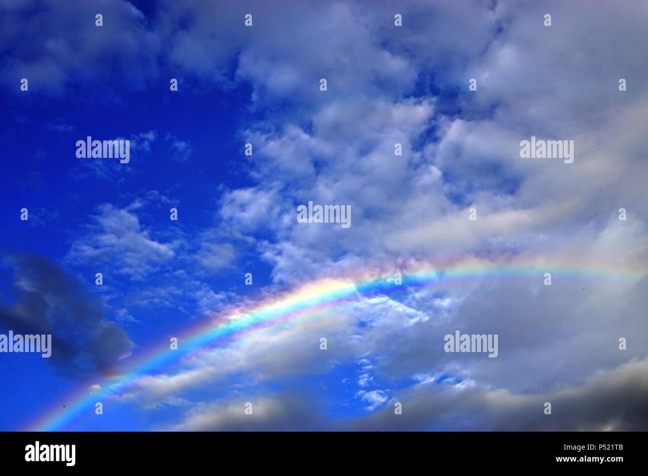 Beautiful rainbow in blue sky among white clouds Stock Photo - Alamy