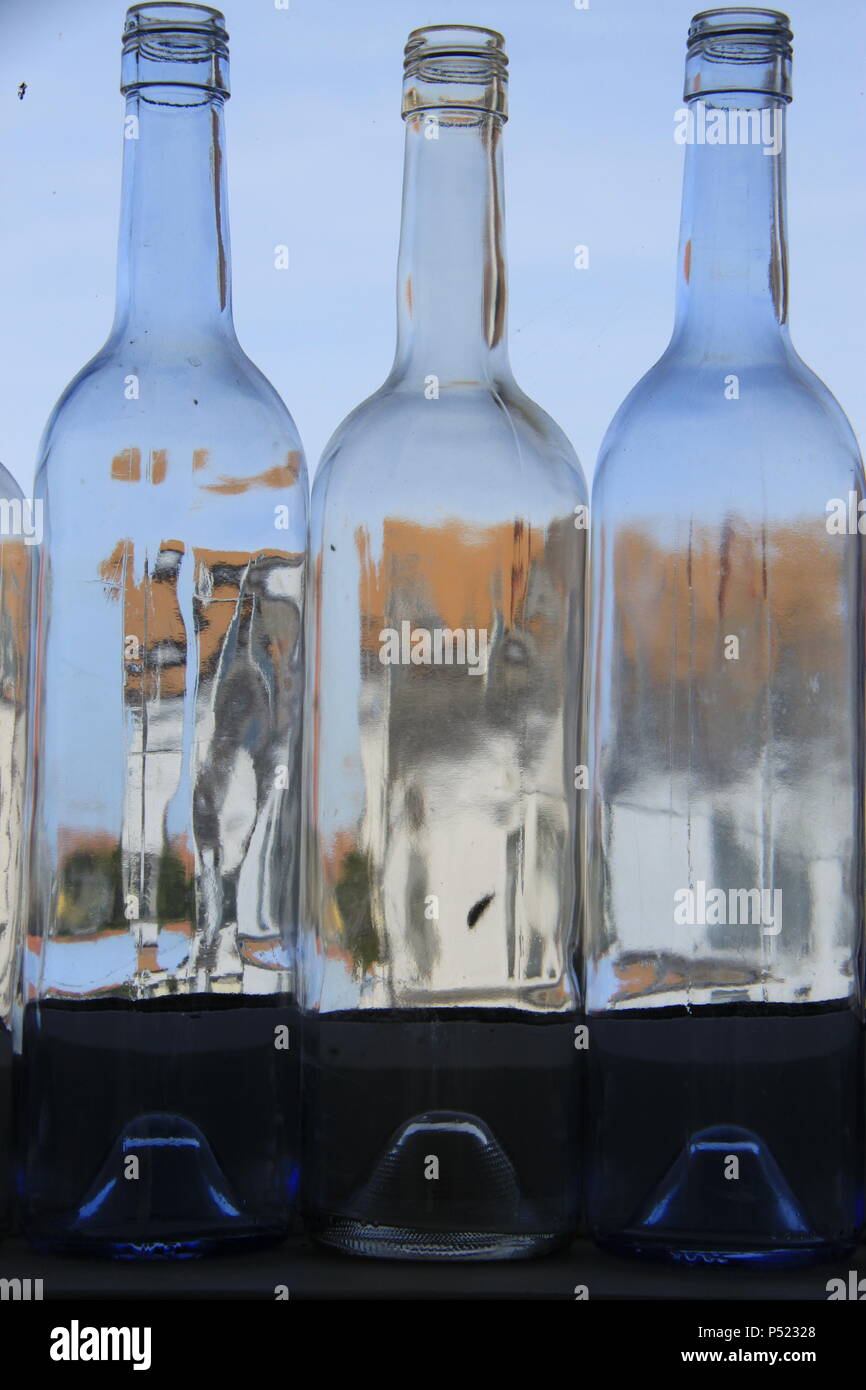 Row of old empty wine bottles on a window sill distorting the sun light ...