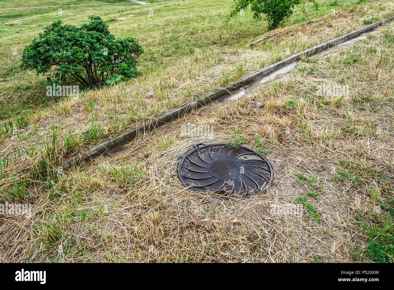 The hatch of the well is closed with a round metal cover. Grass grows ...