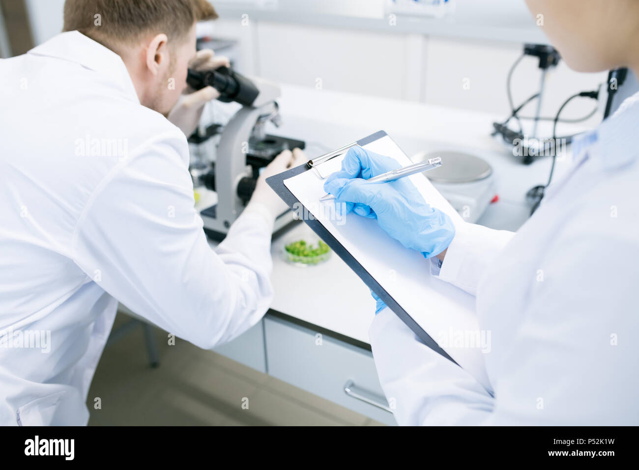 Scientists writing results of research under microscope Stock Photo - Alamy