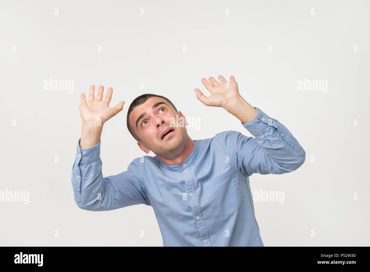 Portrait of young caucasian man in blue shirt raising hands up as if ...