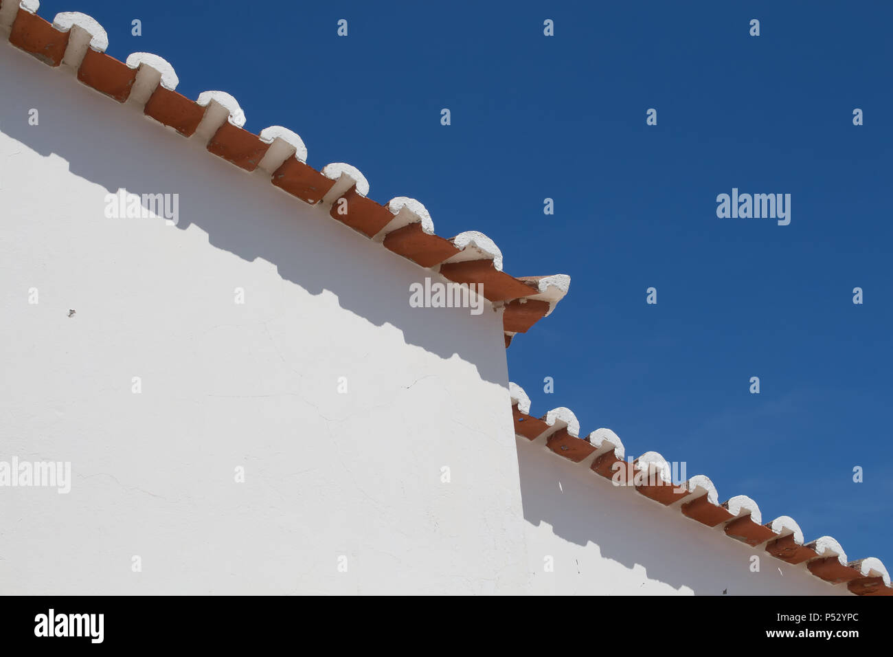 Weathered white facade of a house. Edge of a roof with orange tiles ...