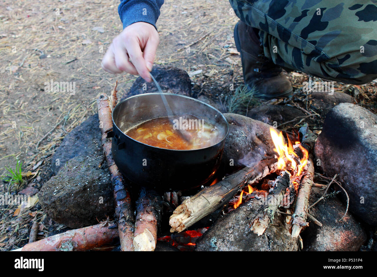 cooking at the stake. stirring with a spoonful of soup in black from ...