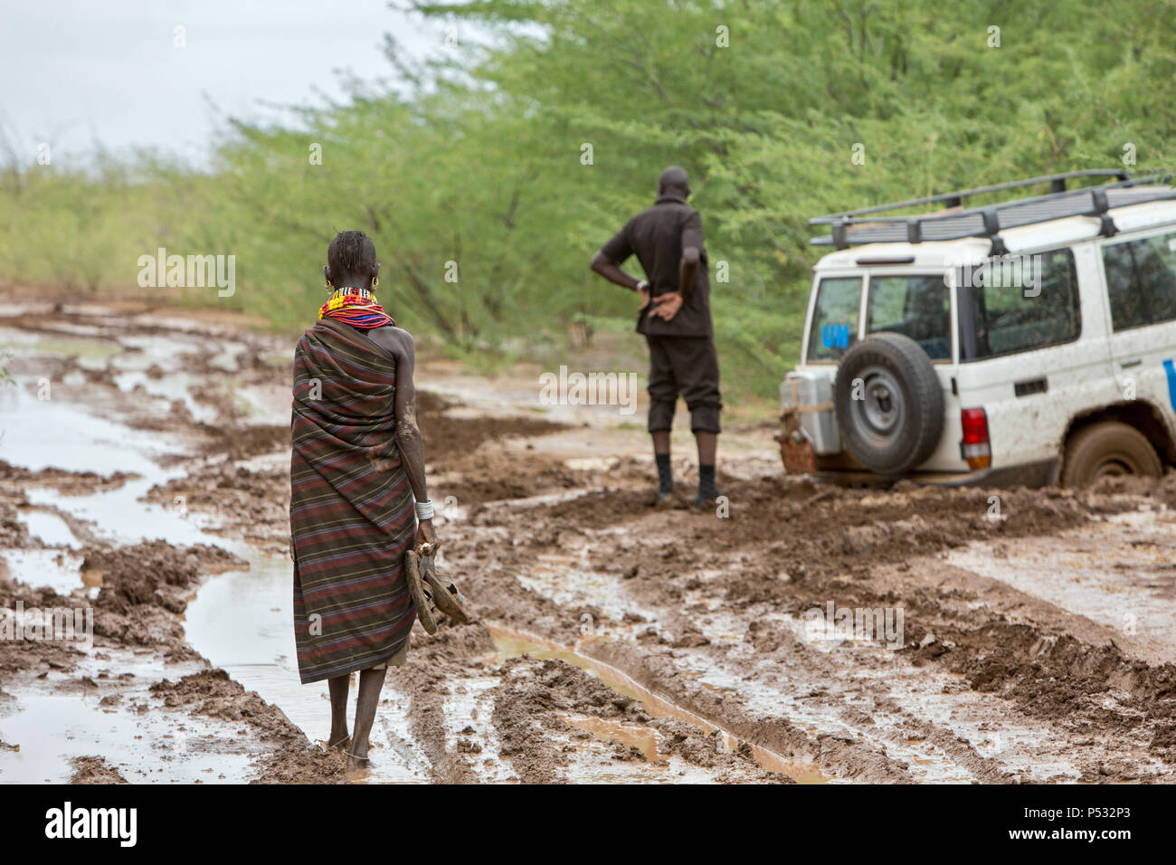 Kakuma, Kenya - A Turkana woman walks barefoot on a dirt road wet with ...