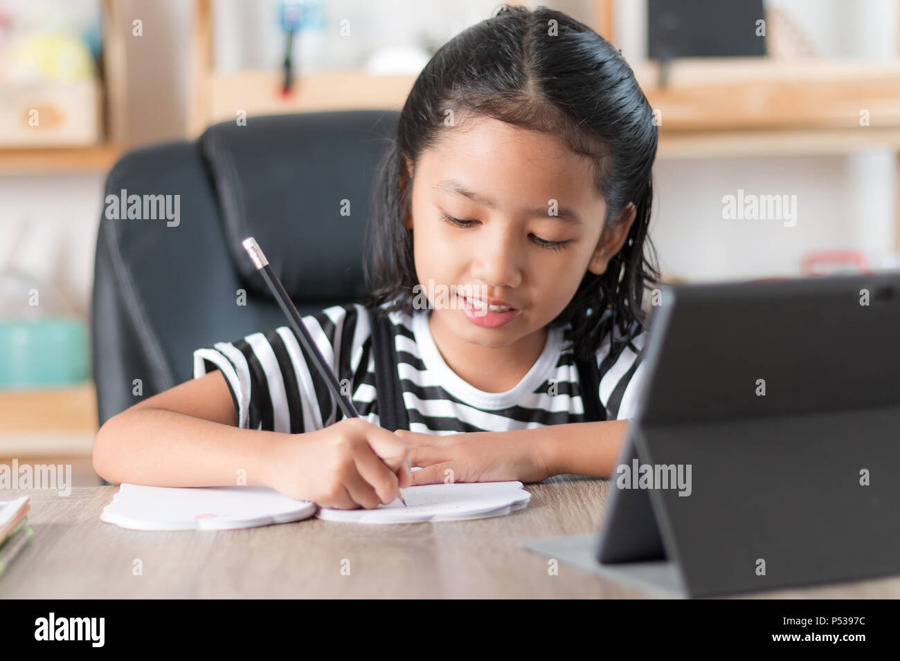 Asian little girl doing homework and pointing finger on wooden table ...