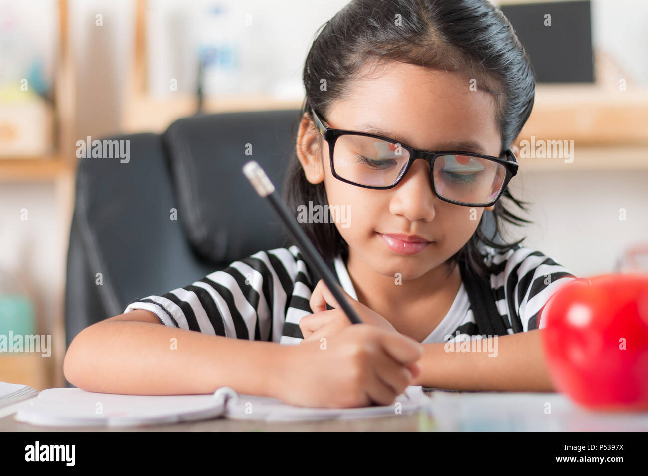 Asian little girl doing homework and pointing finger on wooden table ...