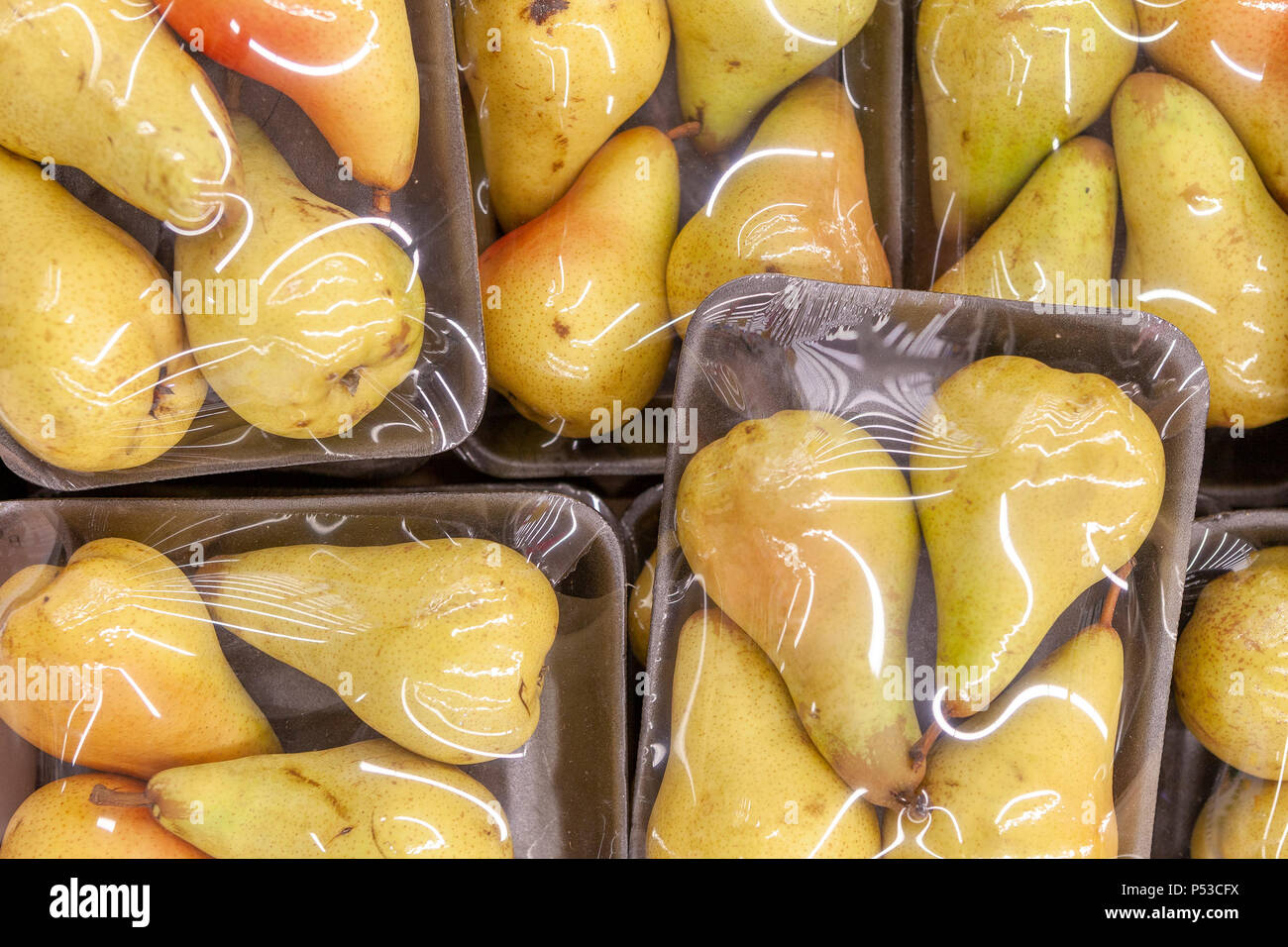 Ripe pears in transparent packaging on plastic pallets in the shop ...