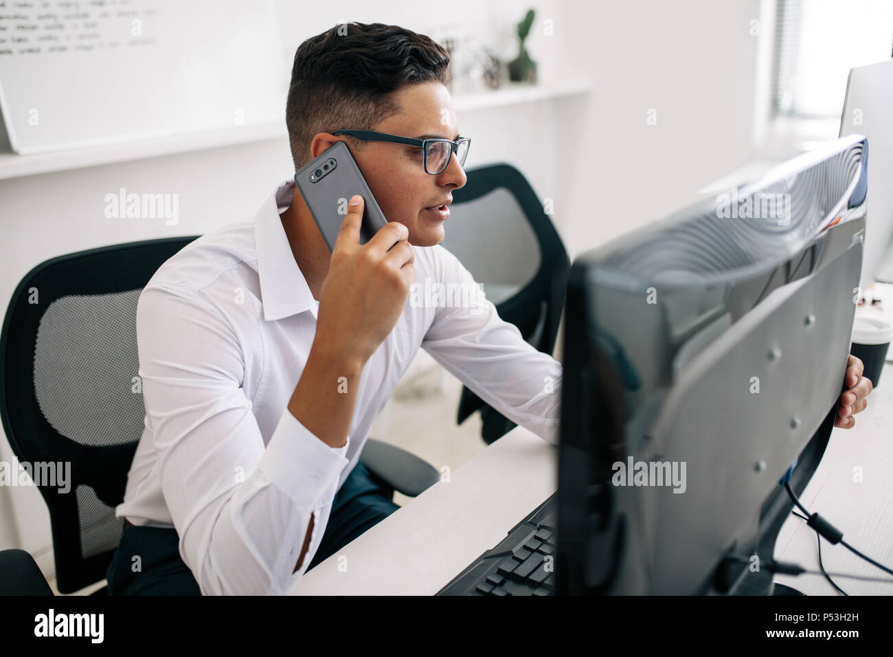 Software developer talking over mobile phone sitting at his office desk ...
