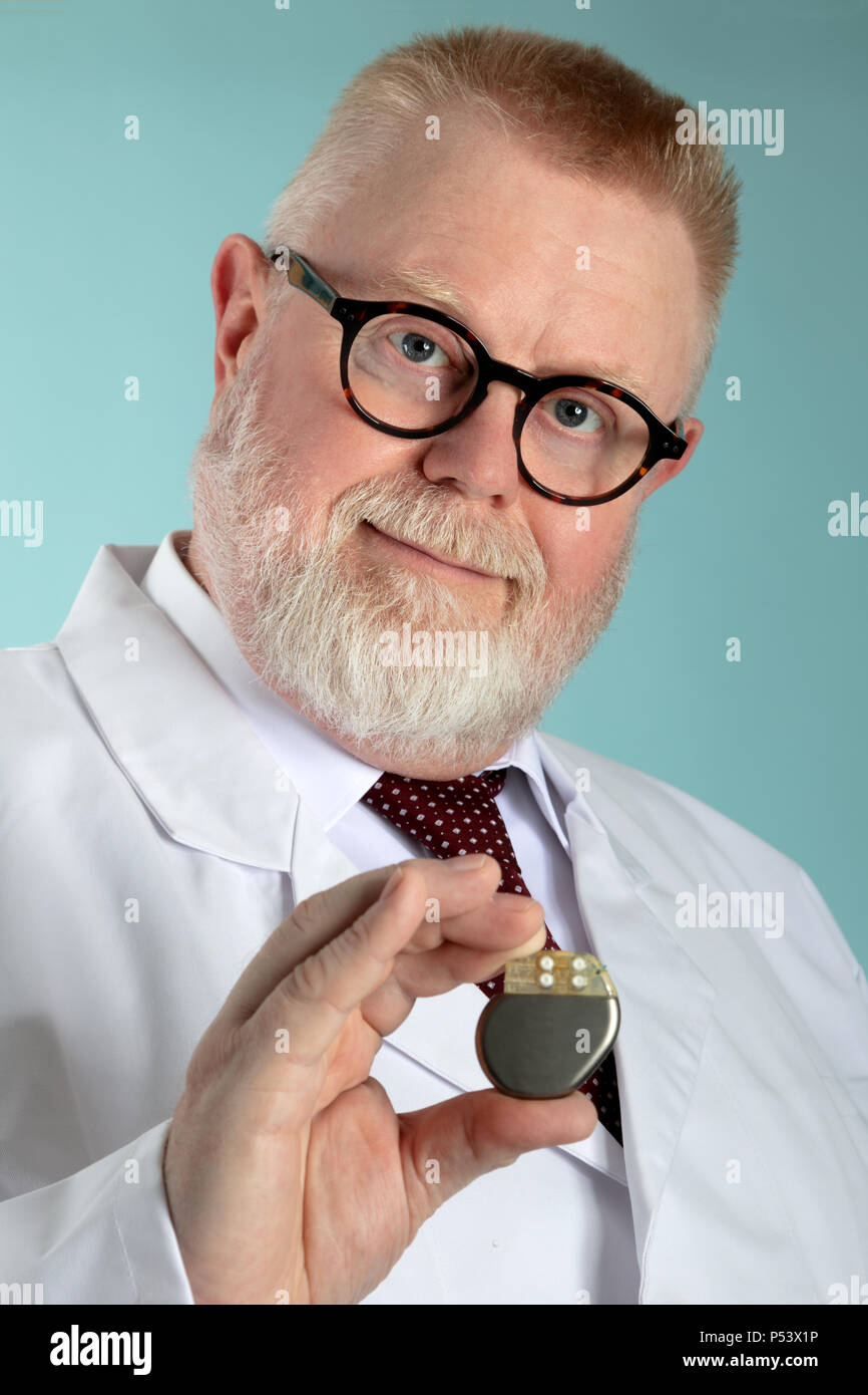 Male Doctor holding Pacemaker in front of camera with blue background ...