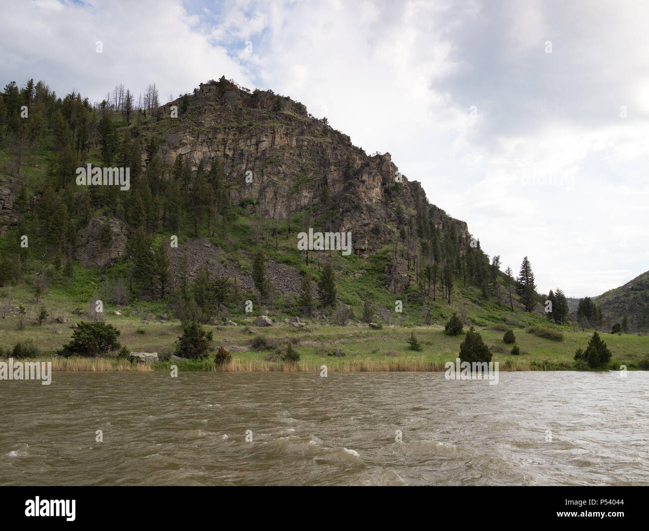 A churning, muddy Madison River near flood stage with a rugged, rocky ...