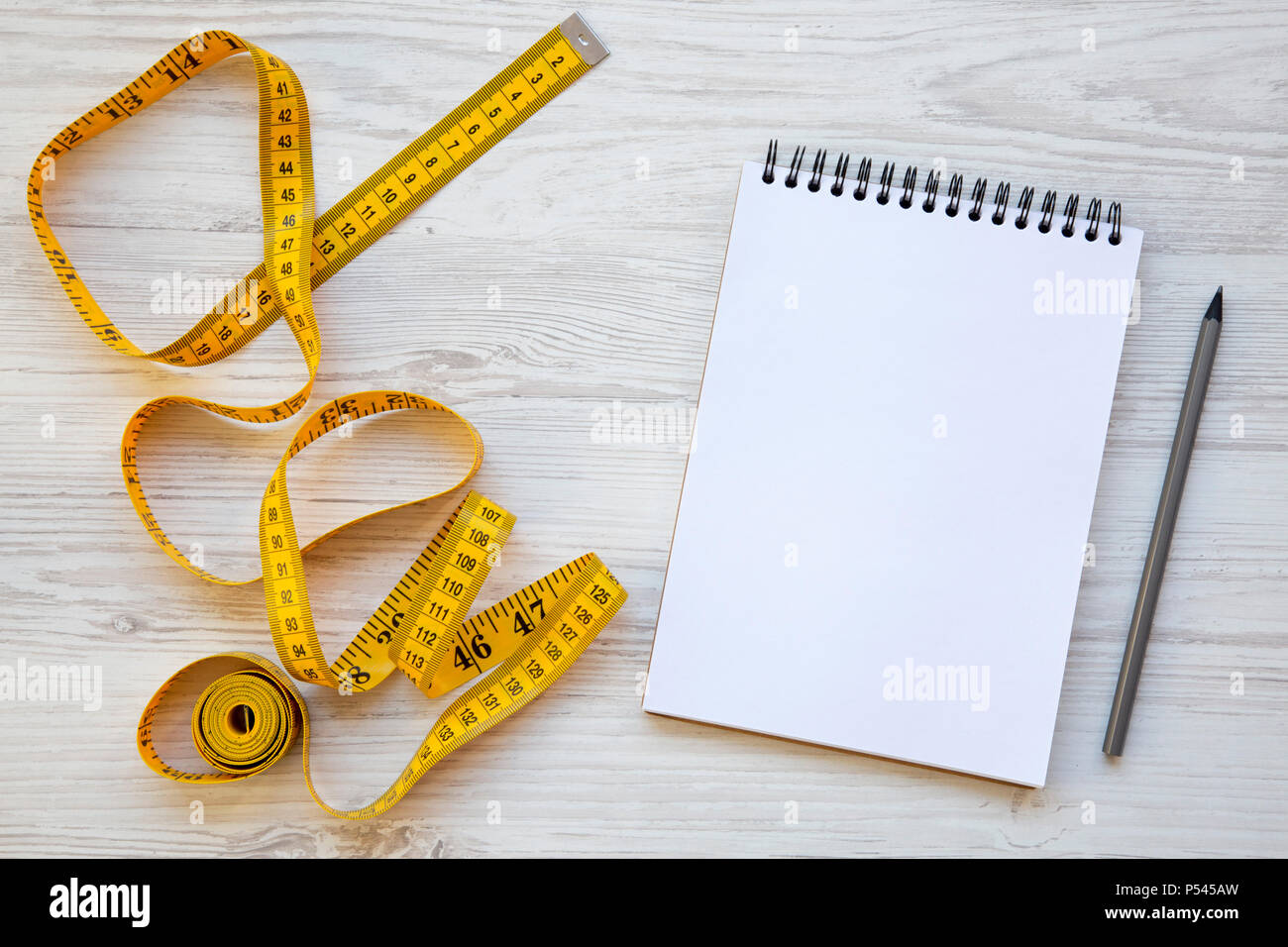 Top view, yellow measuring tape with notepad and pencil on a white ...