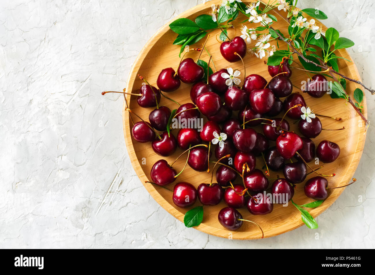 Fresh ripe cherries in a wooden plate. White stone background. Top view ...