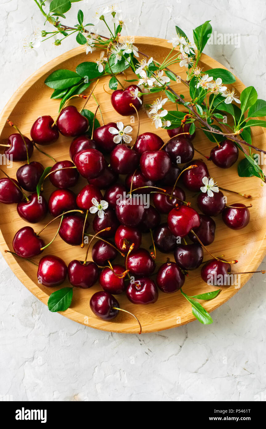 Fresh ripe cherries in a wooden plate. White stone background. Top view ...