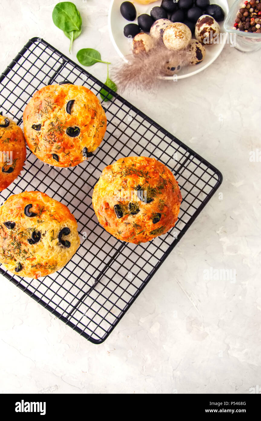Savory muffins with olives and herbs on a wire rack on a white stone ...