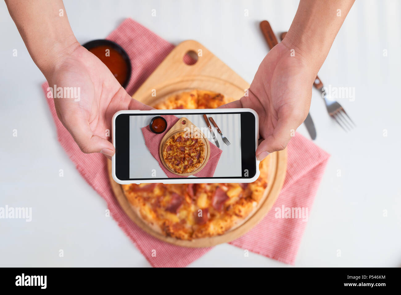 Hand making shot on mobile phone: pizza with pineapple, prosciutto and ...