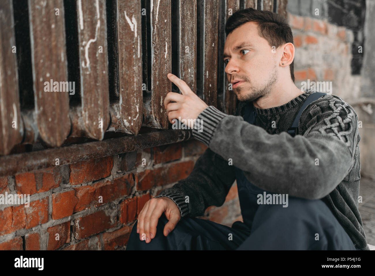 Alone autistic man sitting at the rusty radiator. Alone guy in ...