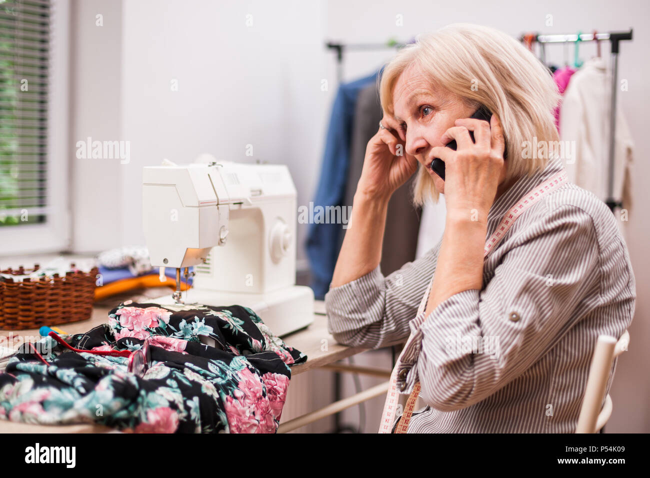 Adult woman is sewing in her studio. She is talking with client Stock ...