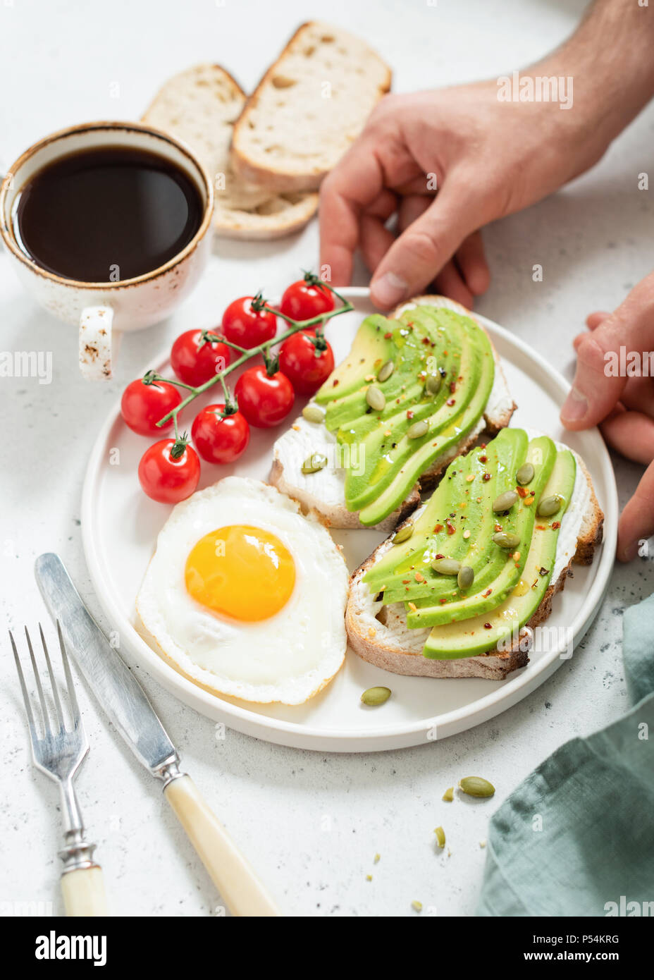 Eating healthy breakfast with avocado, egg, toast and coffee. Hands ...