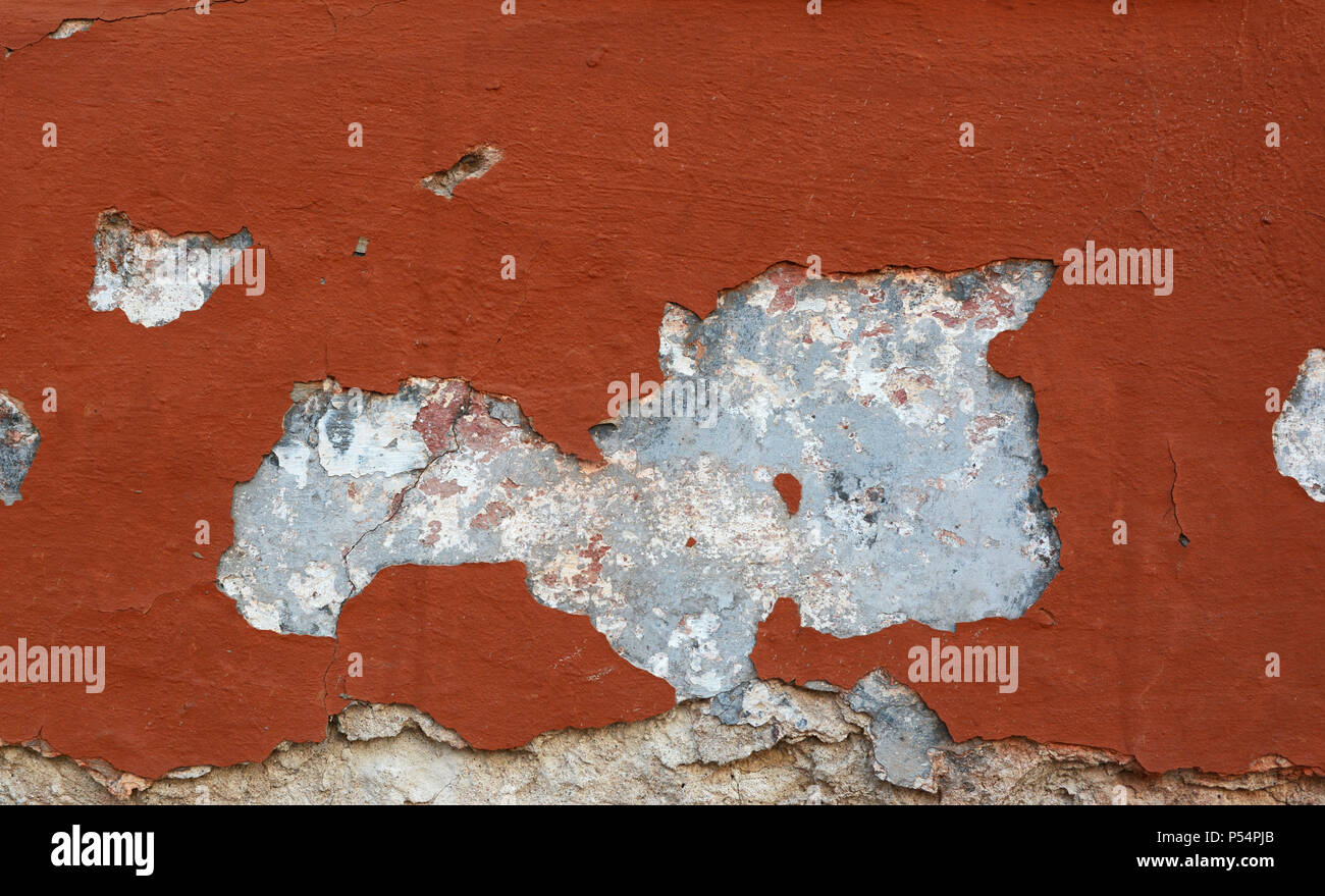 Weathered, damaged wall with red painted render broken away to reveal ...