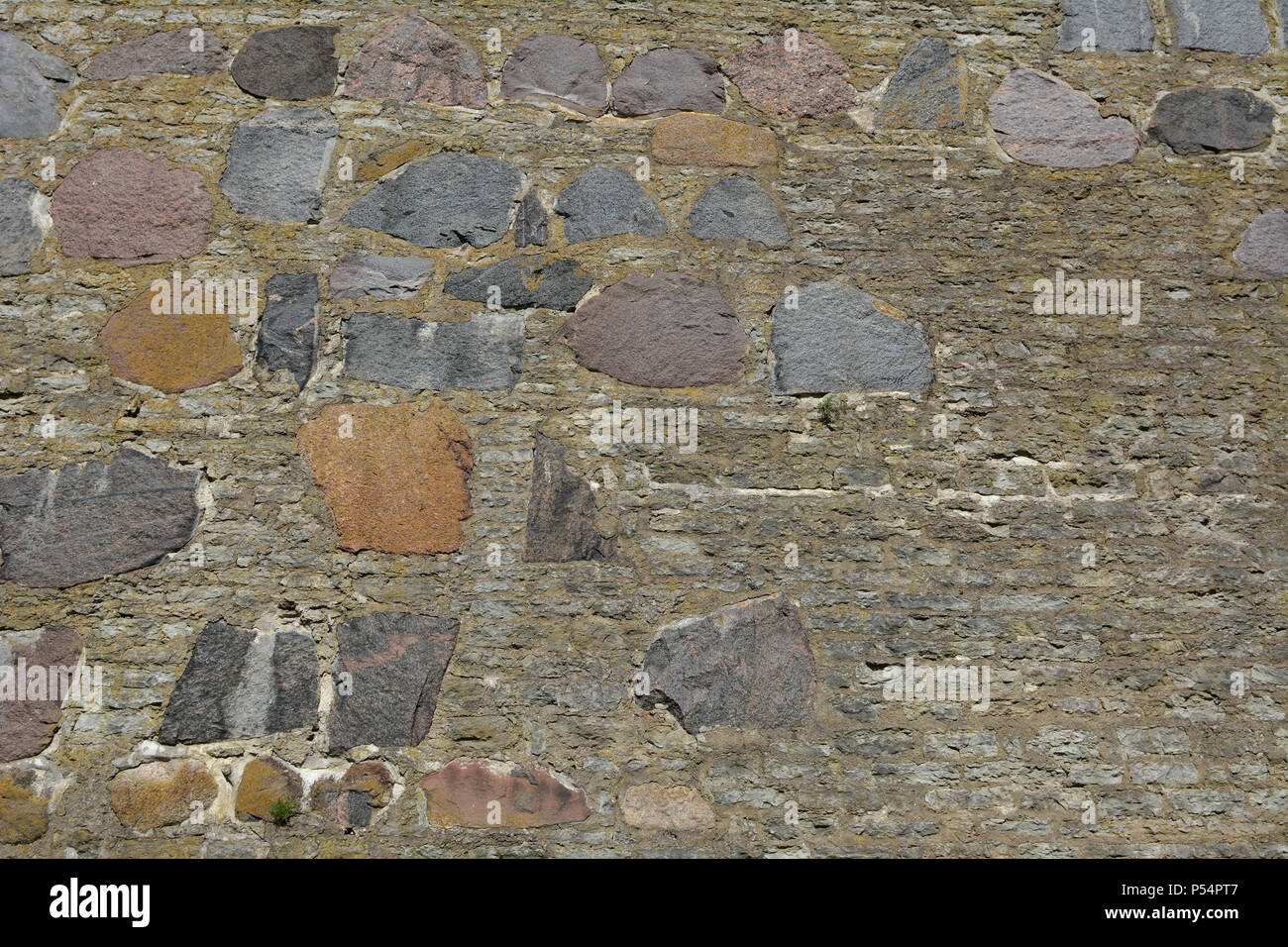 High stone wall with large pieces of coloured stone among smaller grey ...