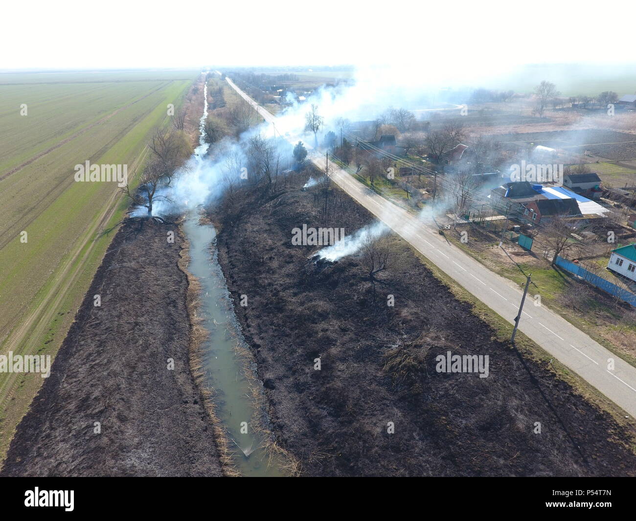 Burning dry grass along the irrigation canal. Smoke and the flame of ...