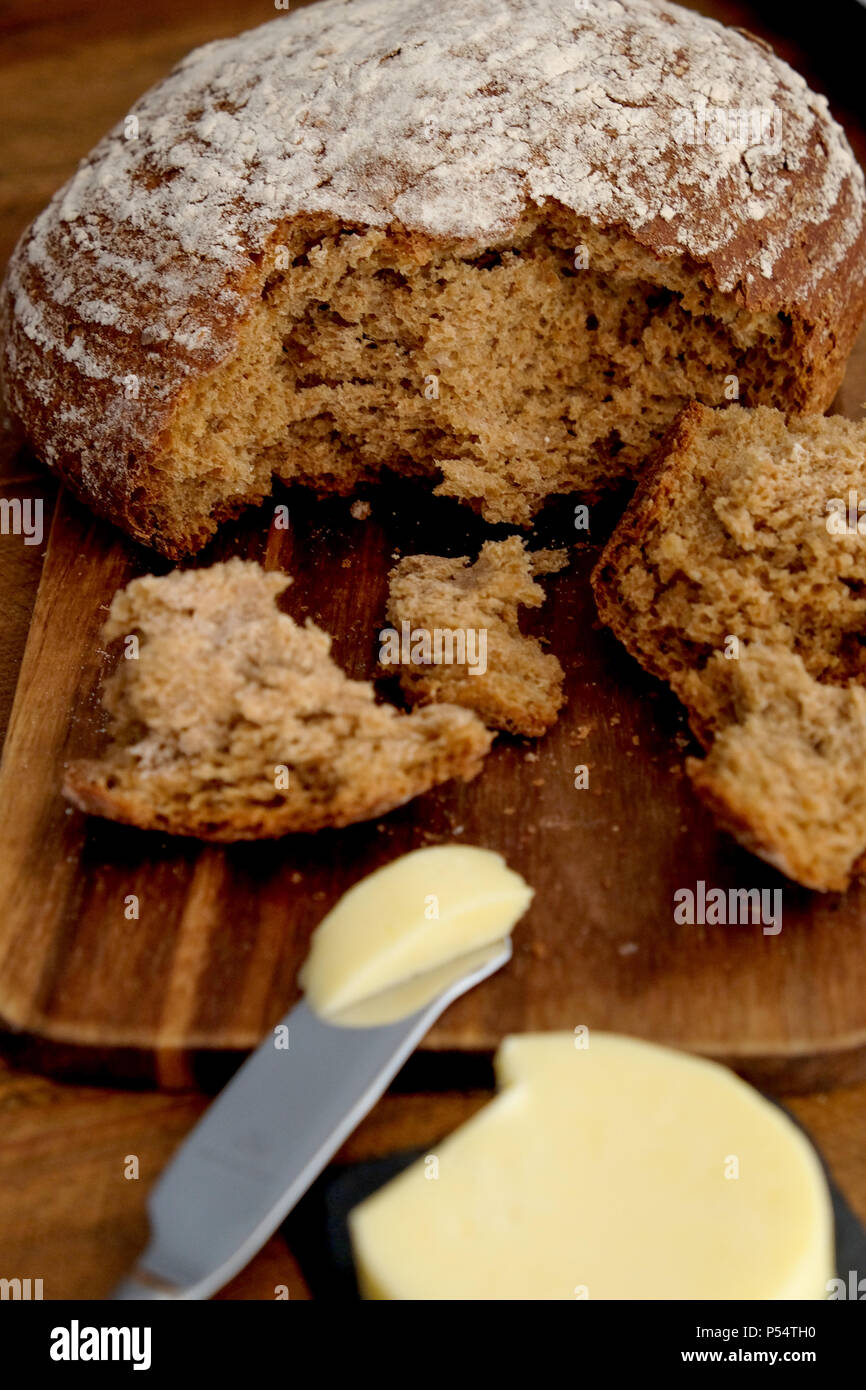 circular shaped brown bread torn apart with a few chunks on a bread ...