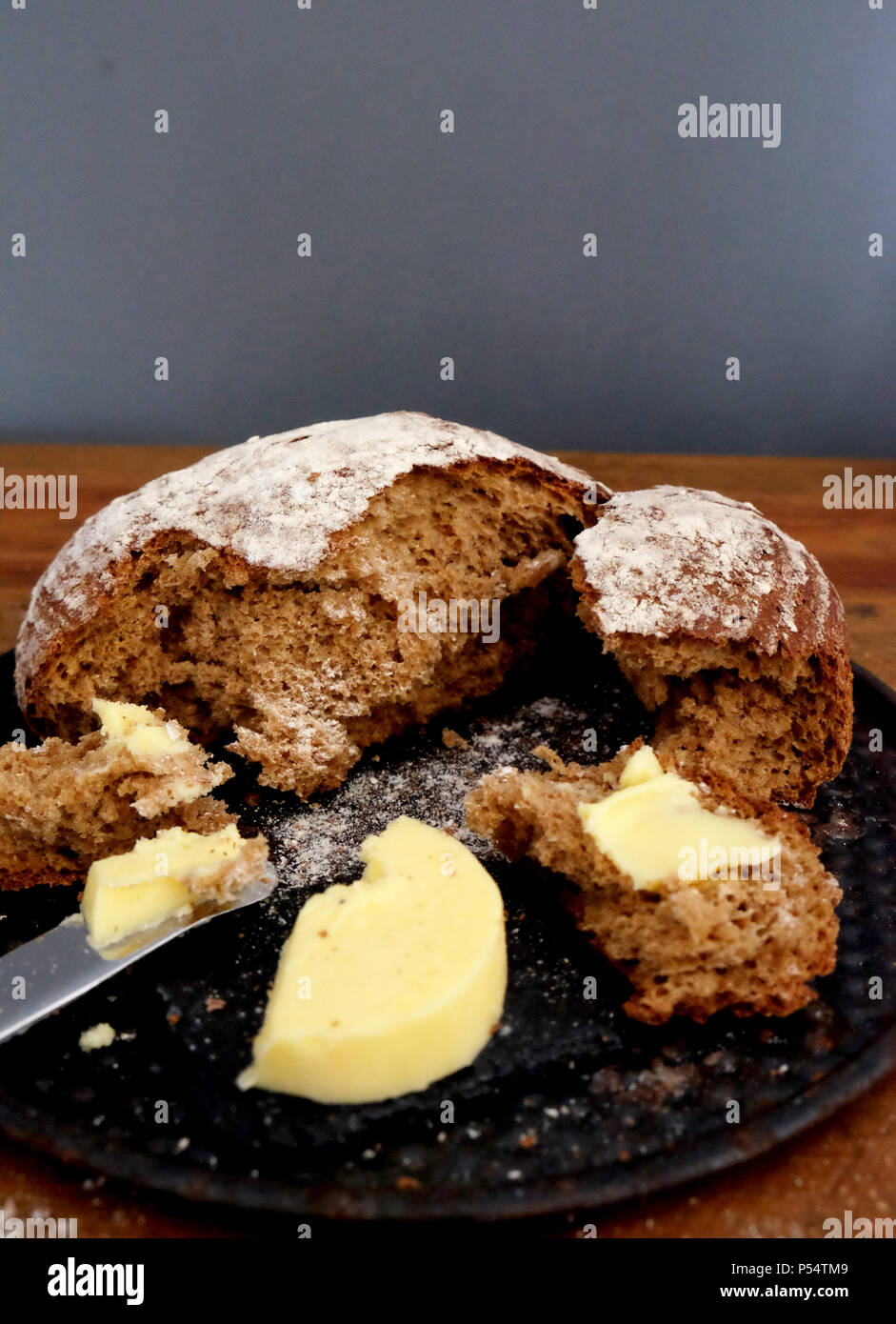 circular shaped brown bread torn apart with a few chunks on a bread ...