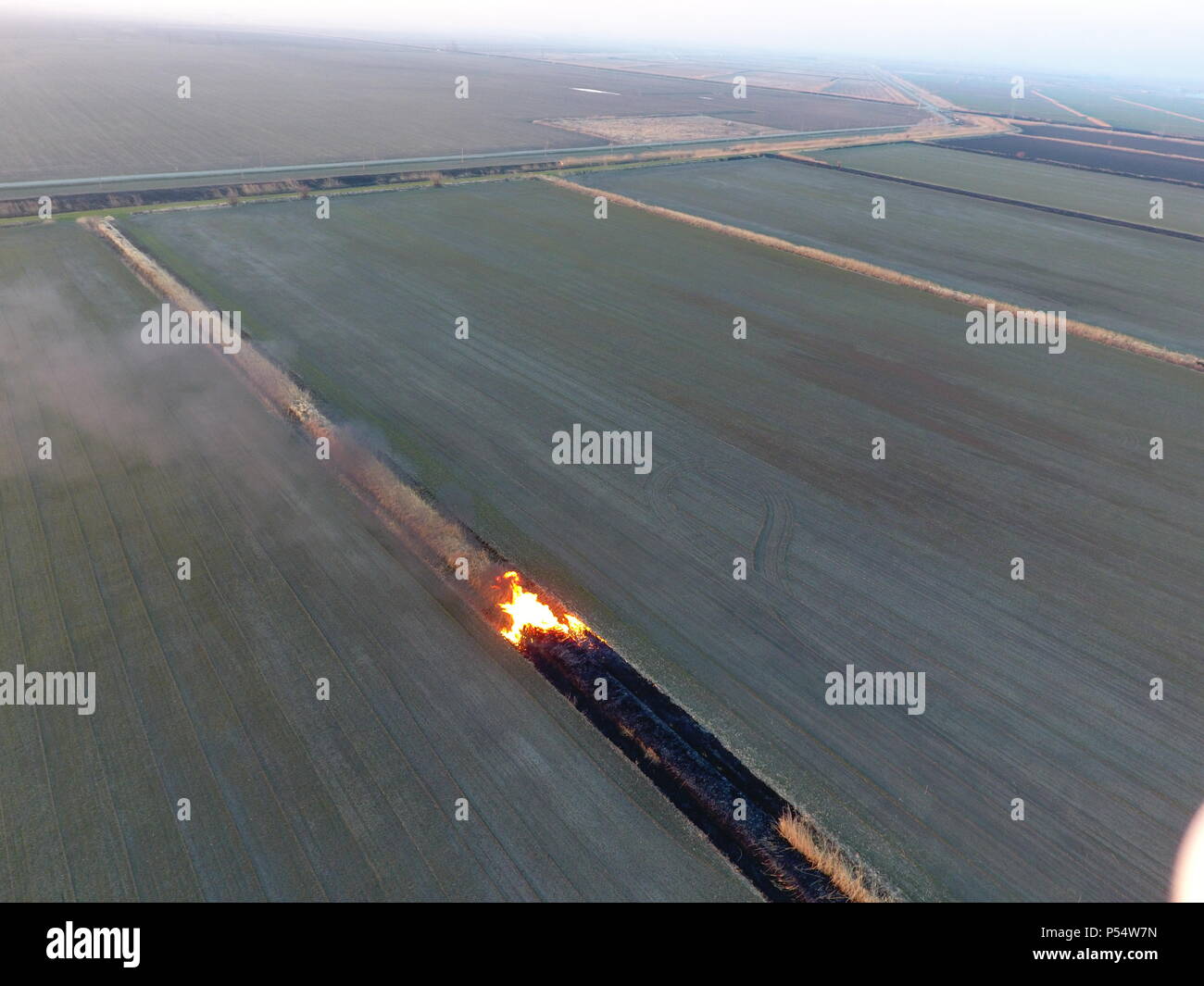 Burning dry grass along the irrigation canal. Smoke and the flame of ...