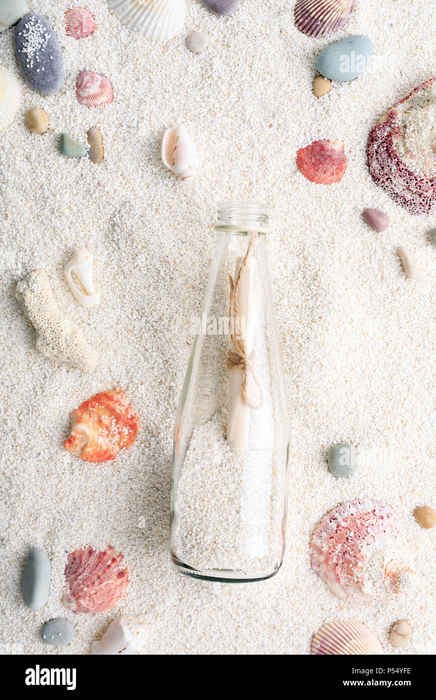 Colorful seashells and sea pebbles on white beach sand & bottle with a ...