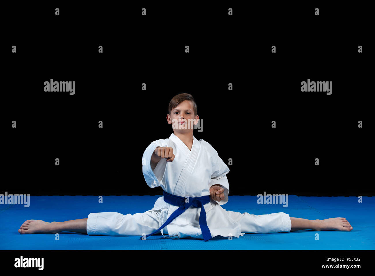 Karate kid wearing white gi and belt in a side split side straddle ...