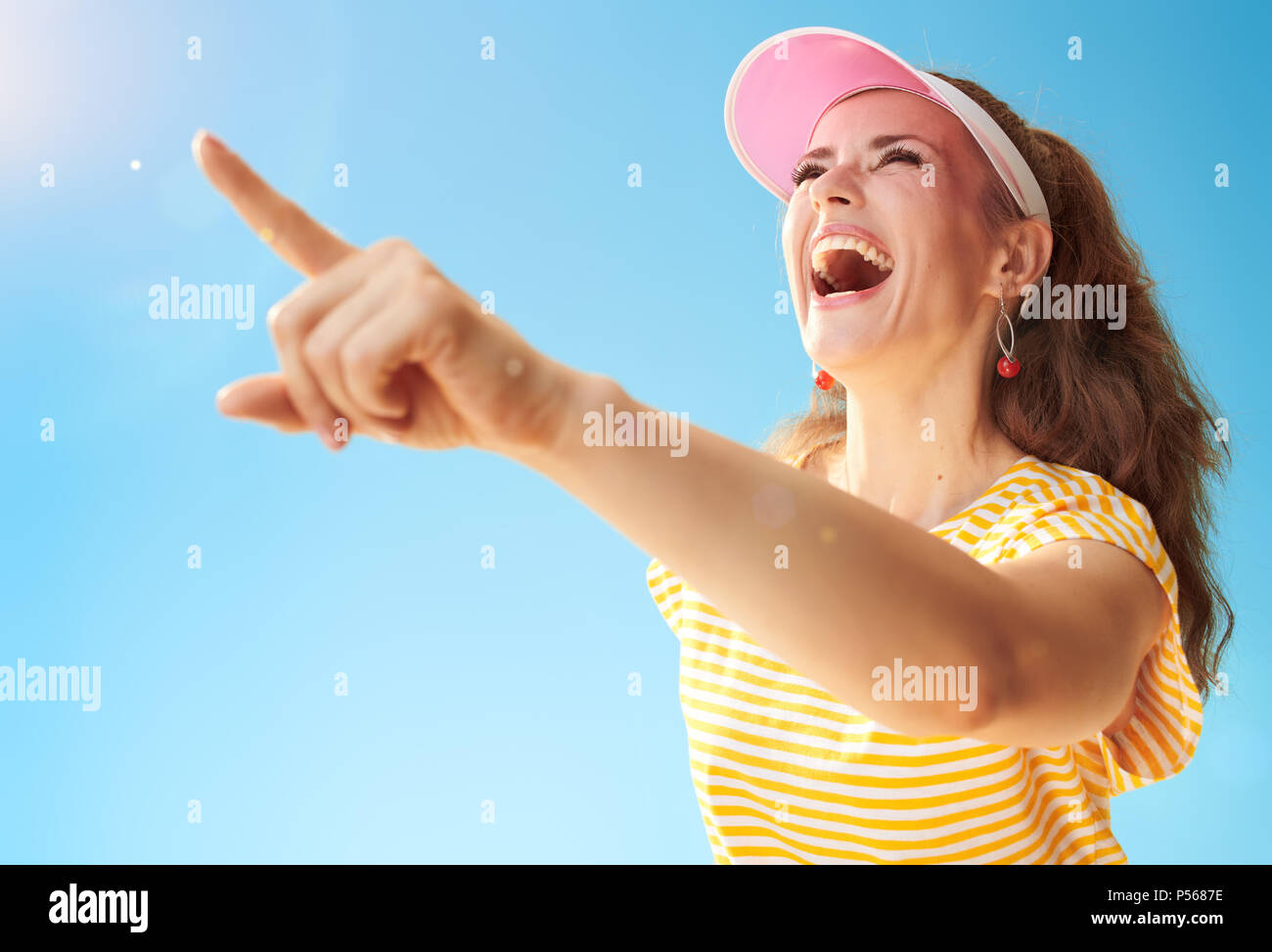 happy active woman in yellow shirt against blue sky pointing at ...