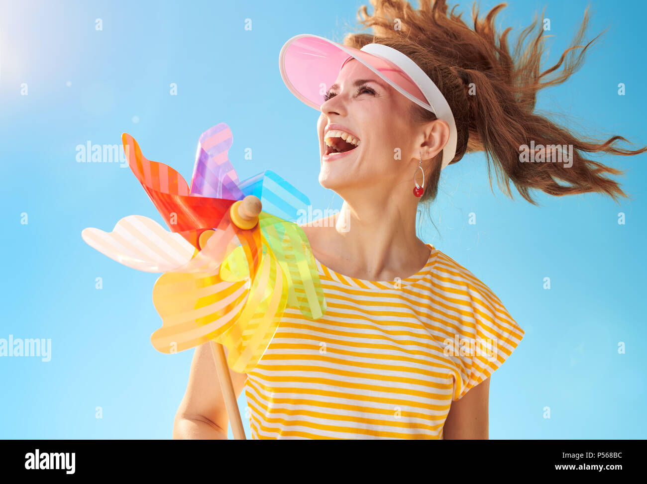 happy fit woman in yellow shirt against blue sky with colorful windmill ...