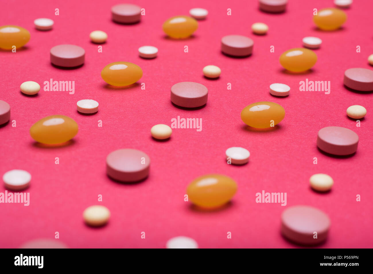 Assortment of various colourful pills on red coloured background ...