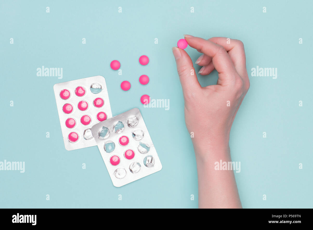 Top view of female hand holding pink prescription pill next to blister ...