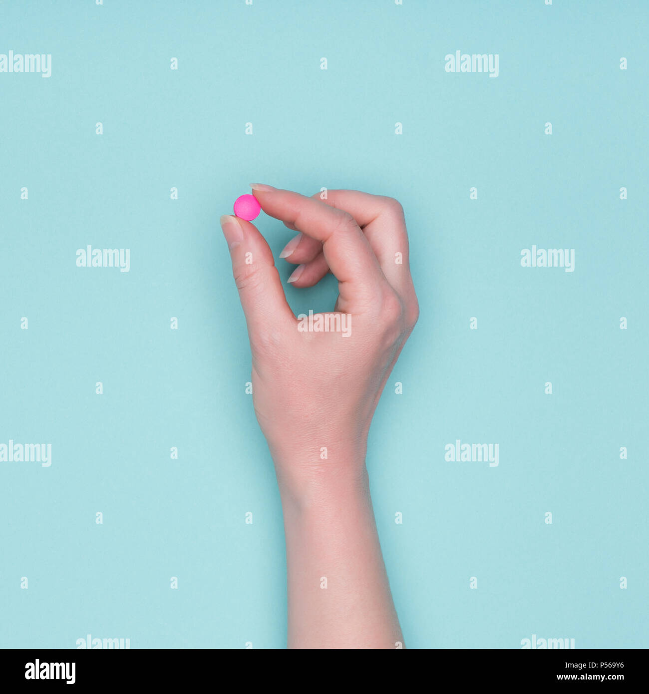 Top view of female hand holding pink prescription pill over pastel blue ...