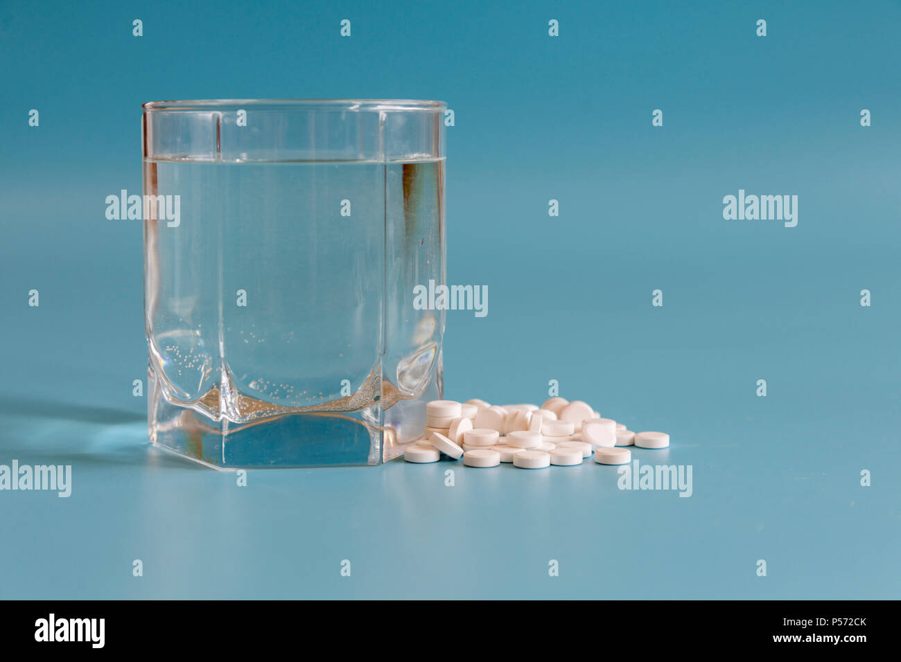 White pills and glass of water on the blue background. Glass of water ...